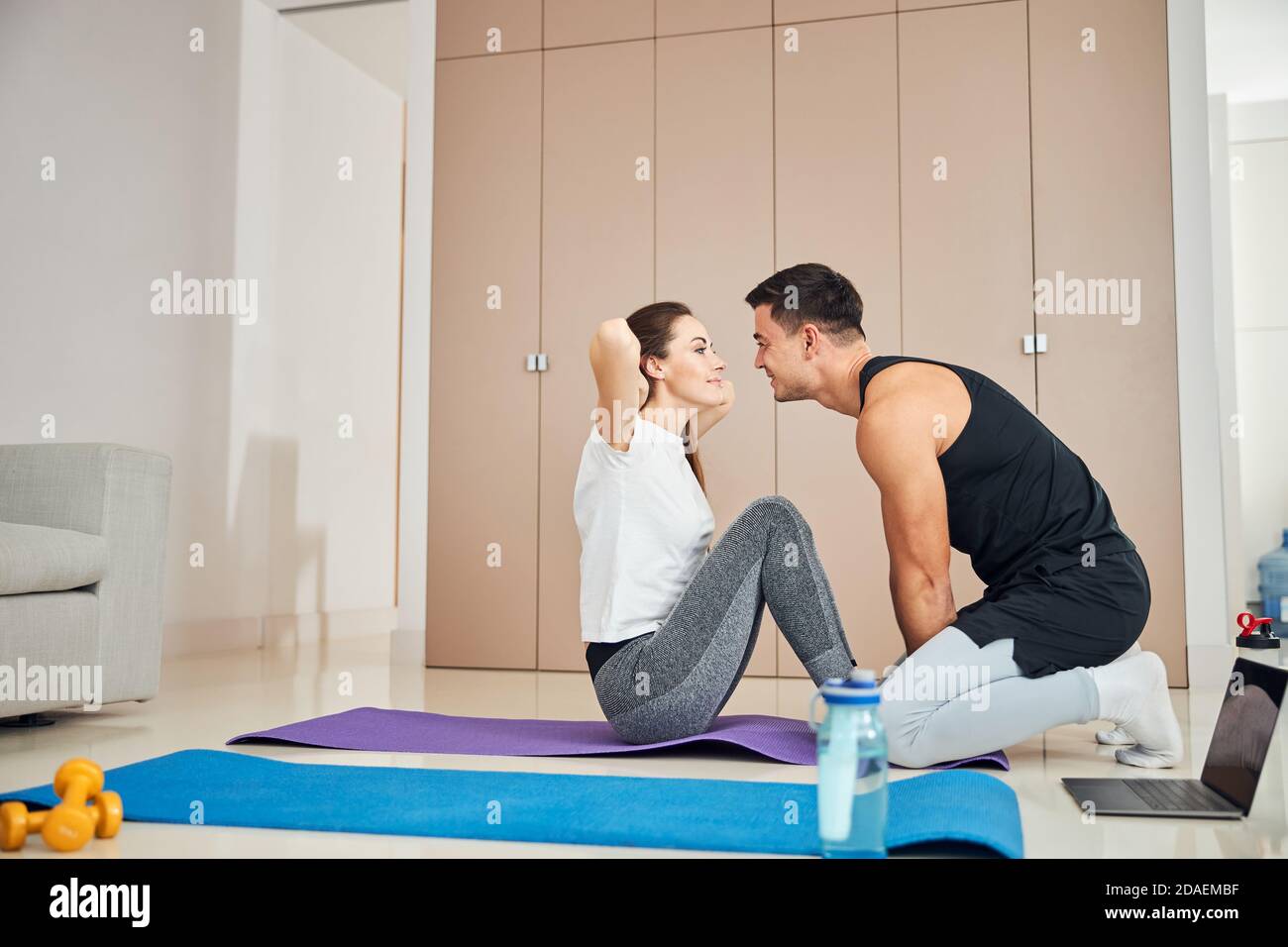 Slim young lady doing sit-ups with help of her boyfriend Stock Photo ...