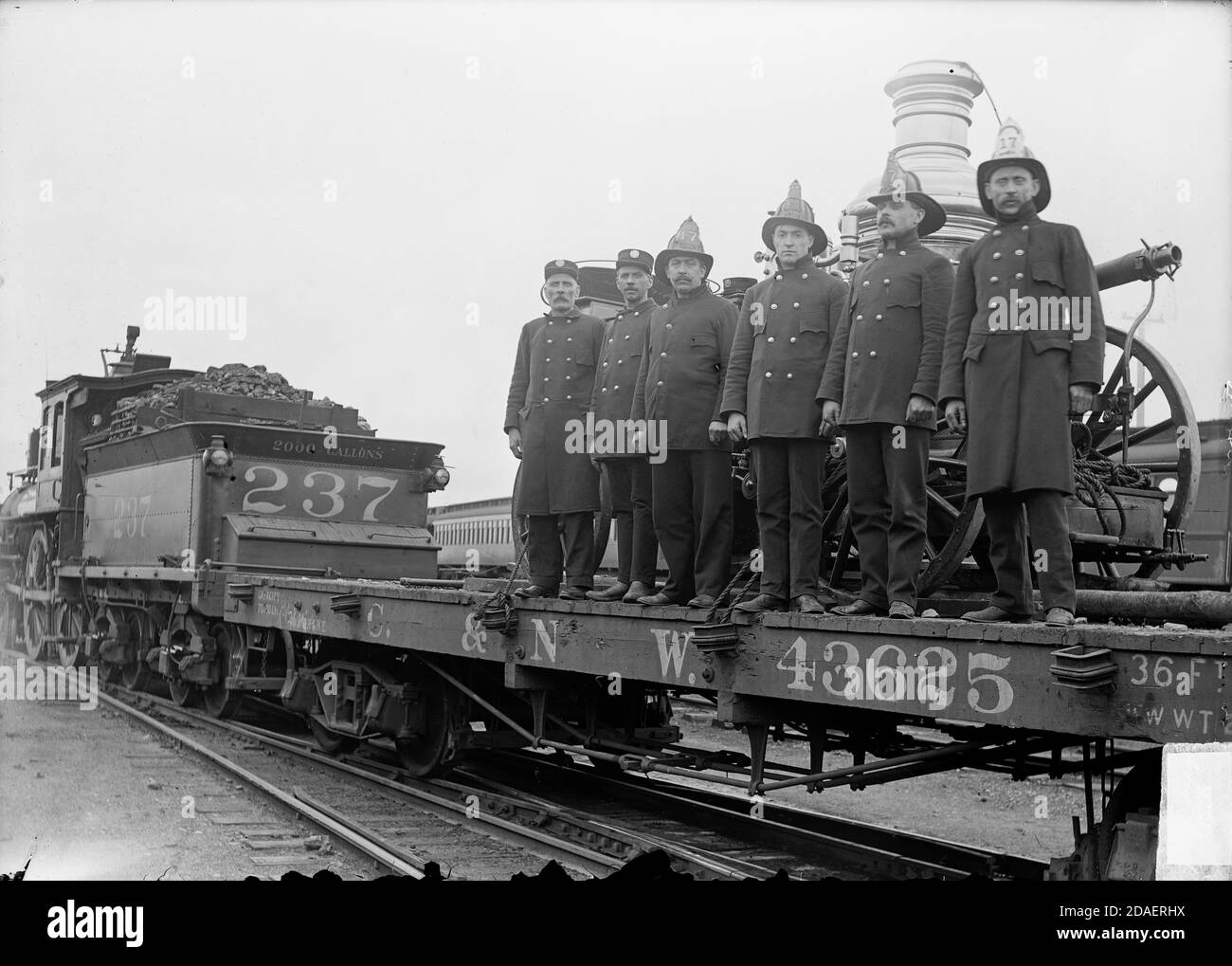 Six firemen standing in front of a fire engine on a train flatcar ...