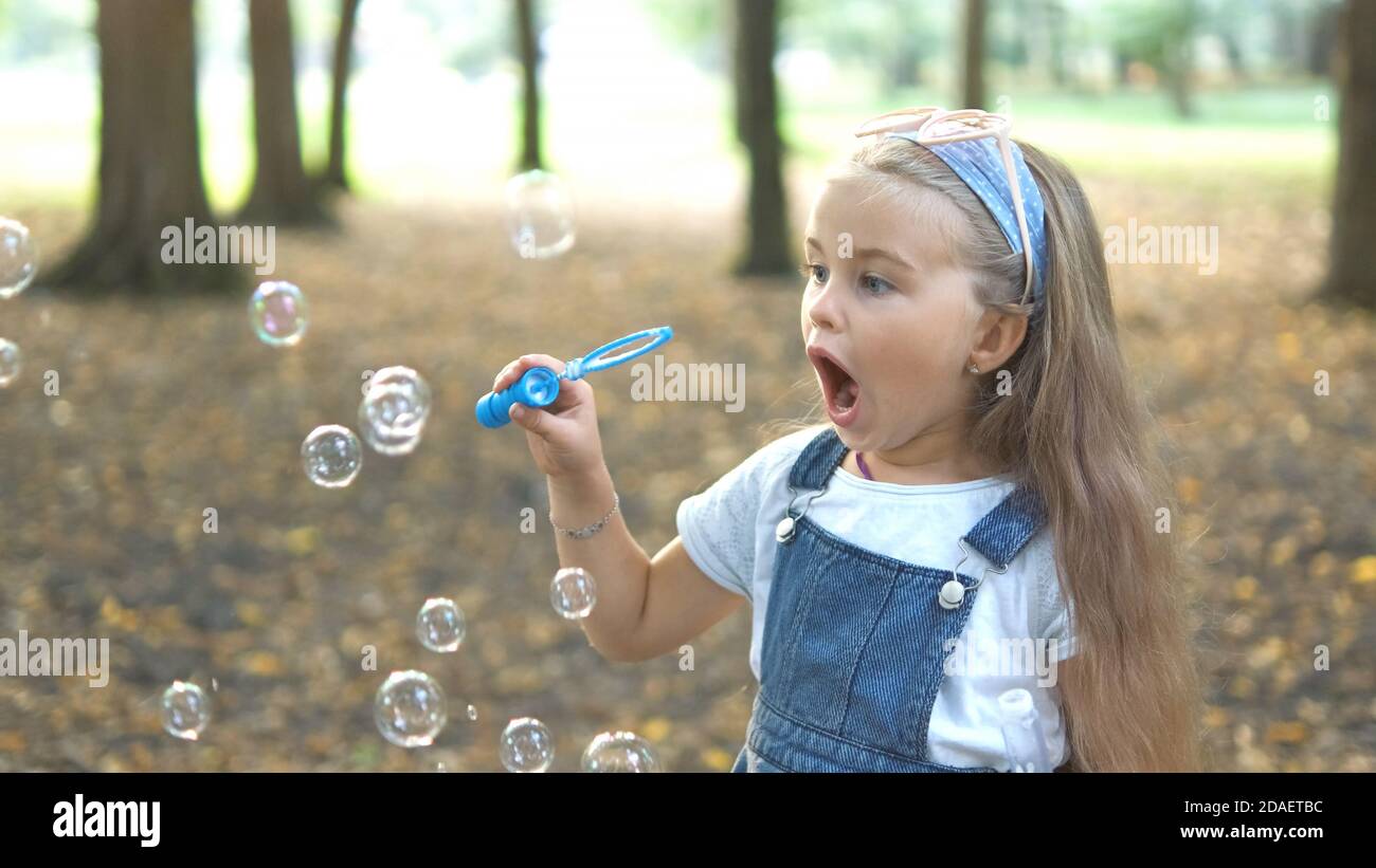 Happy little child girl blowing soap bubbles outside in green park ...