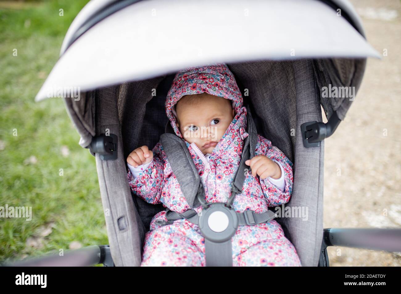 Concerned baby wearing pink flowered jumpsuit inside a stroller Stock ...