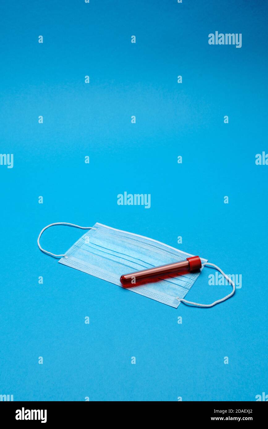 Protective medical face masks and test tube with blood sample on a blue ...