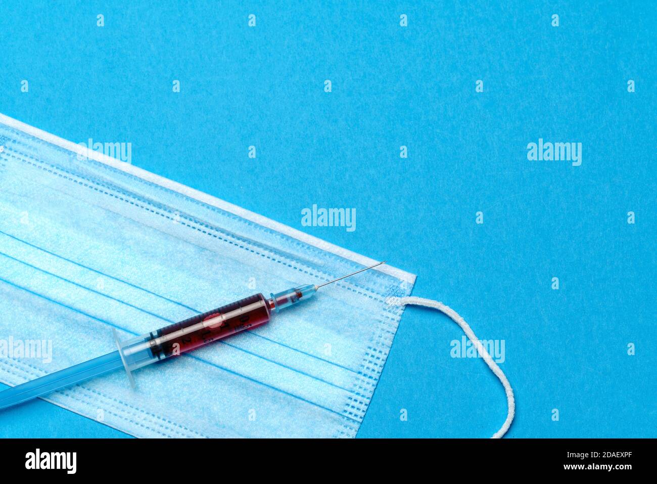 Syringe and disposable face mask to prevent COVID-19 virus on blue ...
