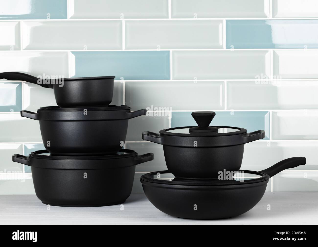 New black cookware against blue tile wall Stock Photo - Alamy