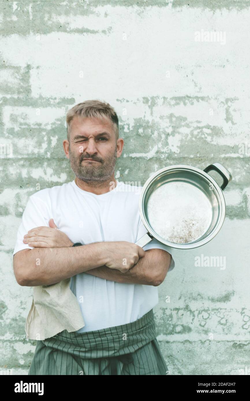 Stylish caucasian attractive chef in an apron and with a steel frying ...