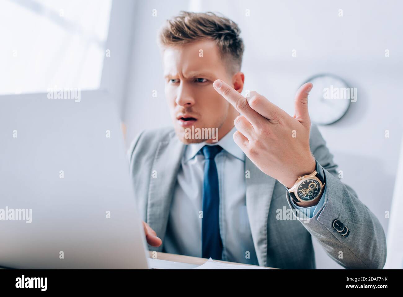 Angry businessman showing middle finger while using laptop on blurred ...