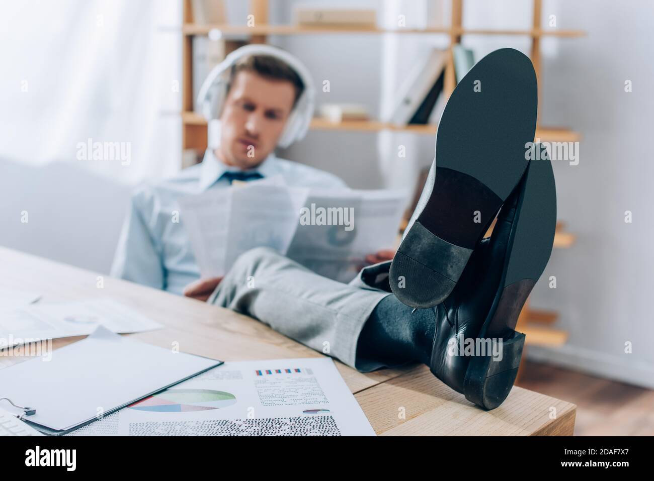 Businessman with legs on table using headphones and working with ...
