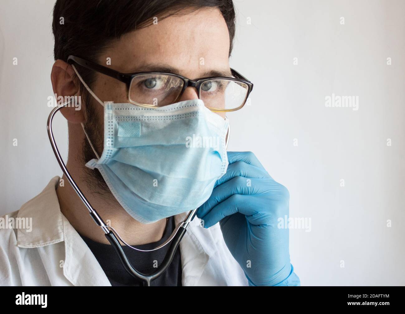 A young handsome doctor wearing glasses and a medical face mask puts on ...