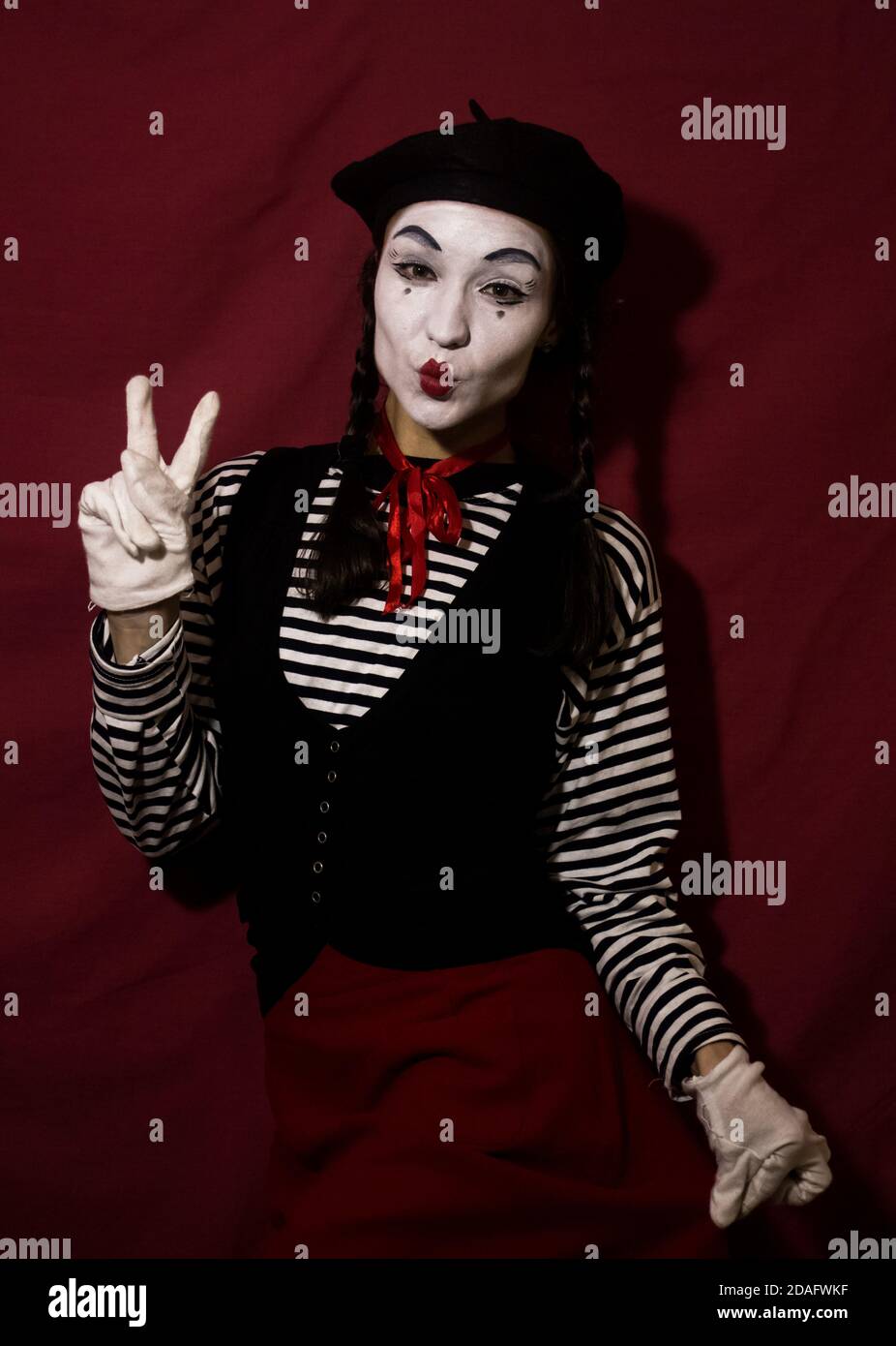 Beautiful mime girl grimaces and shows a victory sign with her hand ...
