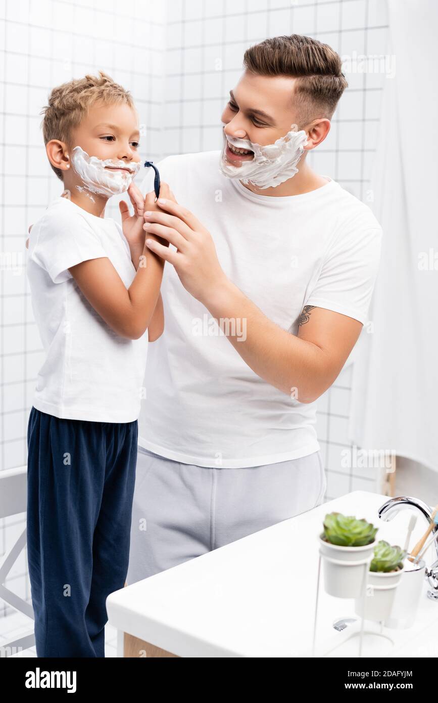 Smiling father looking at son with shaving foam holding safety razor ...
