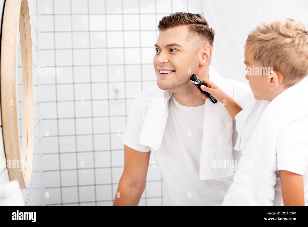 Son holding electric razor and shaving face of father smiling and ...
