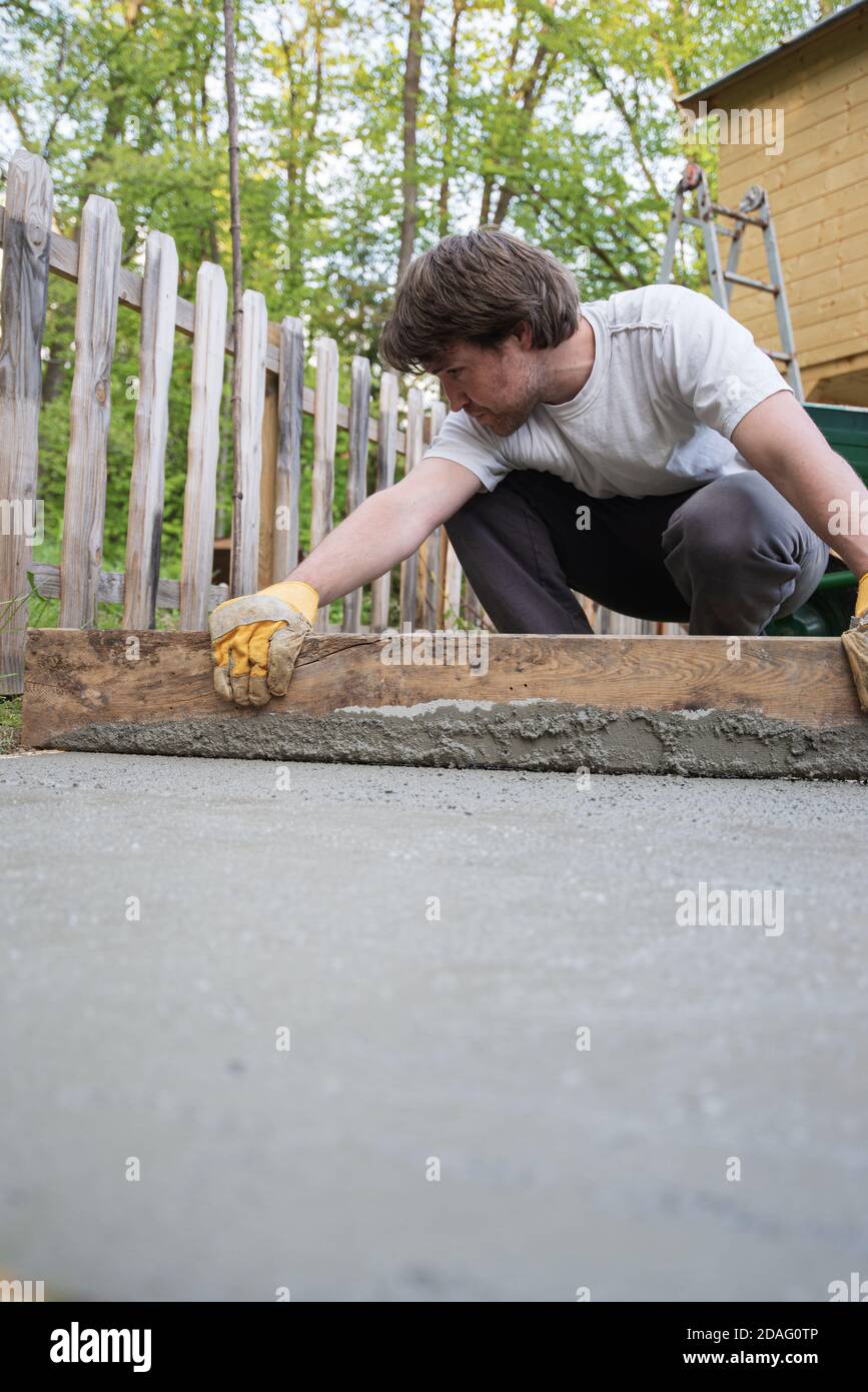 Low angle view of a man leveling fresh cement to build a foundation in ...
