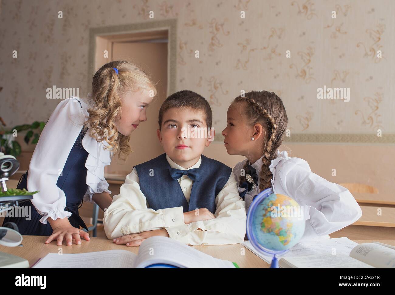 two girls and a boy at school at a Desk studying biology and geography ...