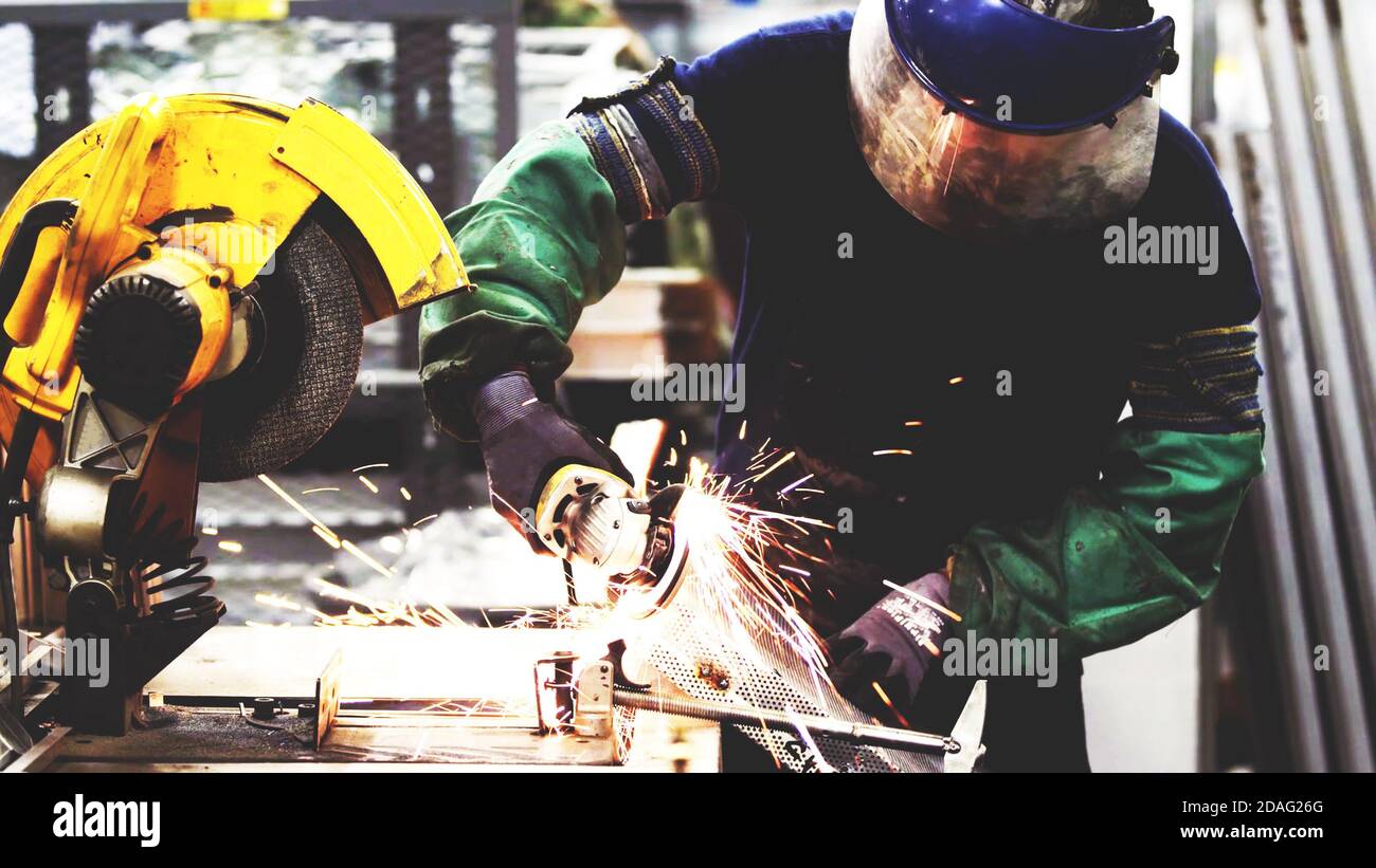 Heavy industry worker cutting steel with electric grinder machine in ...