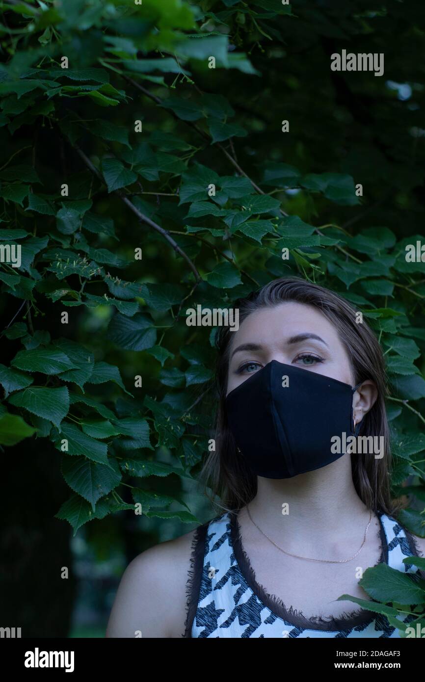 Pretty young blonde woman in medical black face mask. in a bush, forest ...