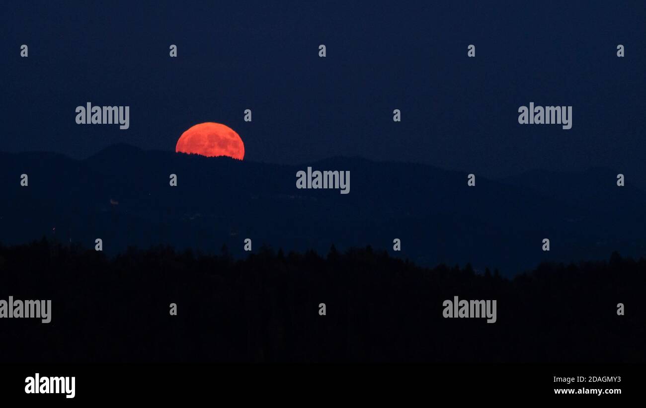 huge orange full moon rising into the night sky behind a mountain ridge ...