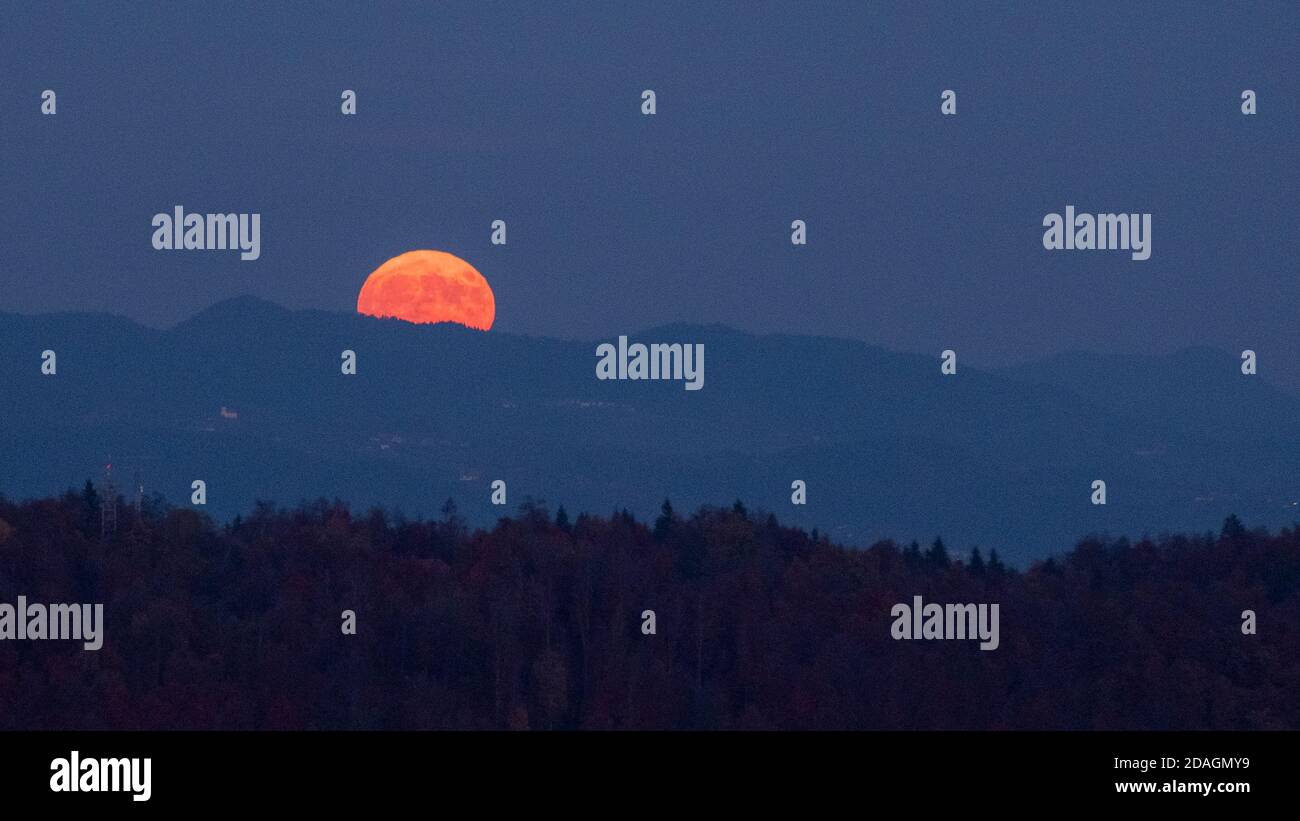 huge orange full moon rising behind a mountain ridge illuminating misty ...