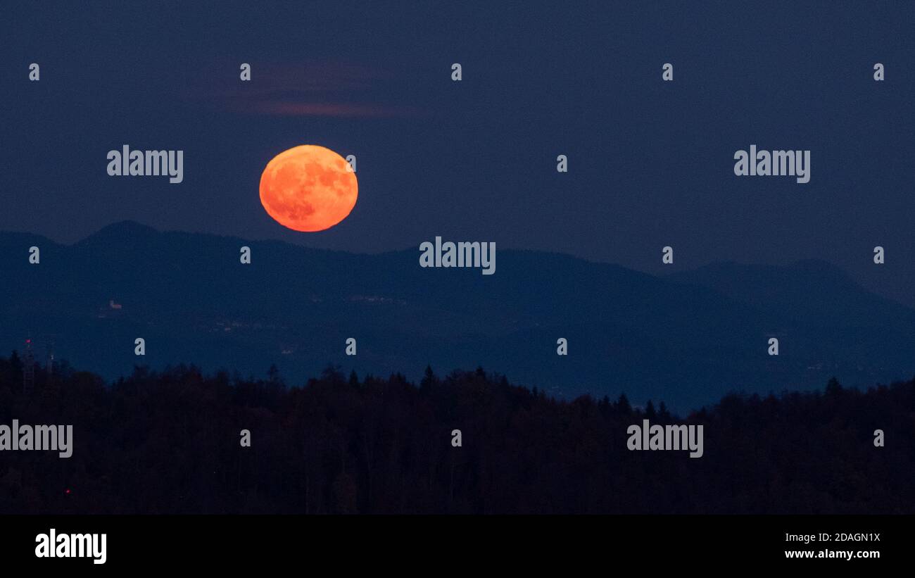 huge orange full moon rising into the night sky behind a mountain ridge ...