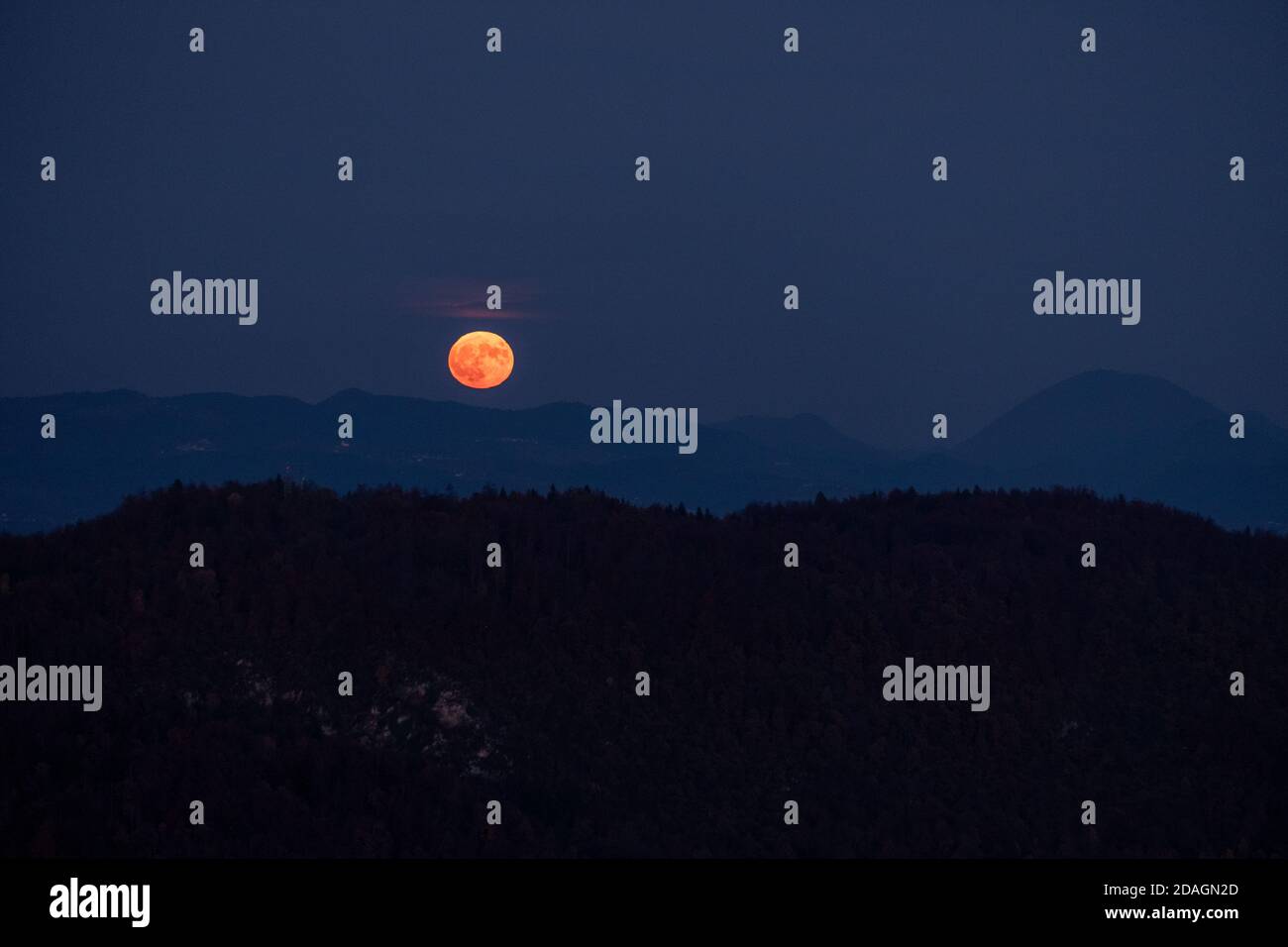 huge orange full moon rising into the night sky behind a mountain ridge ...