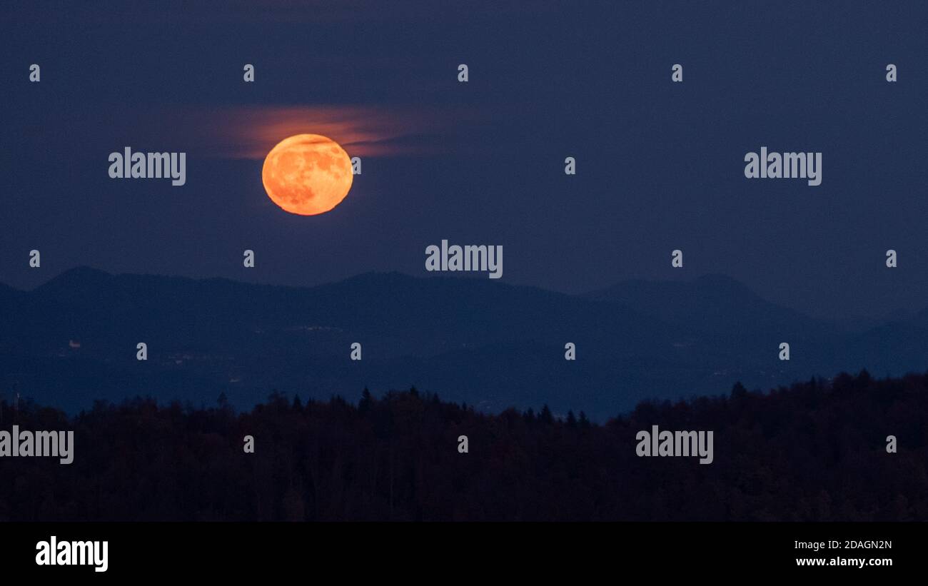 huge orange full moon rising behind a mountain ridge illuminating misty ...