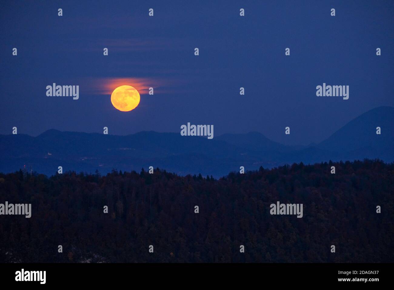 huge orange full moon rising behind a mountain ridge illuminating misty ...