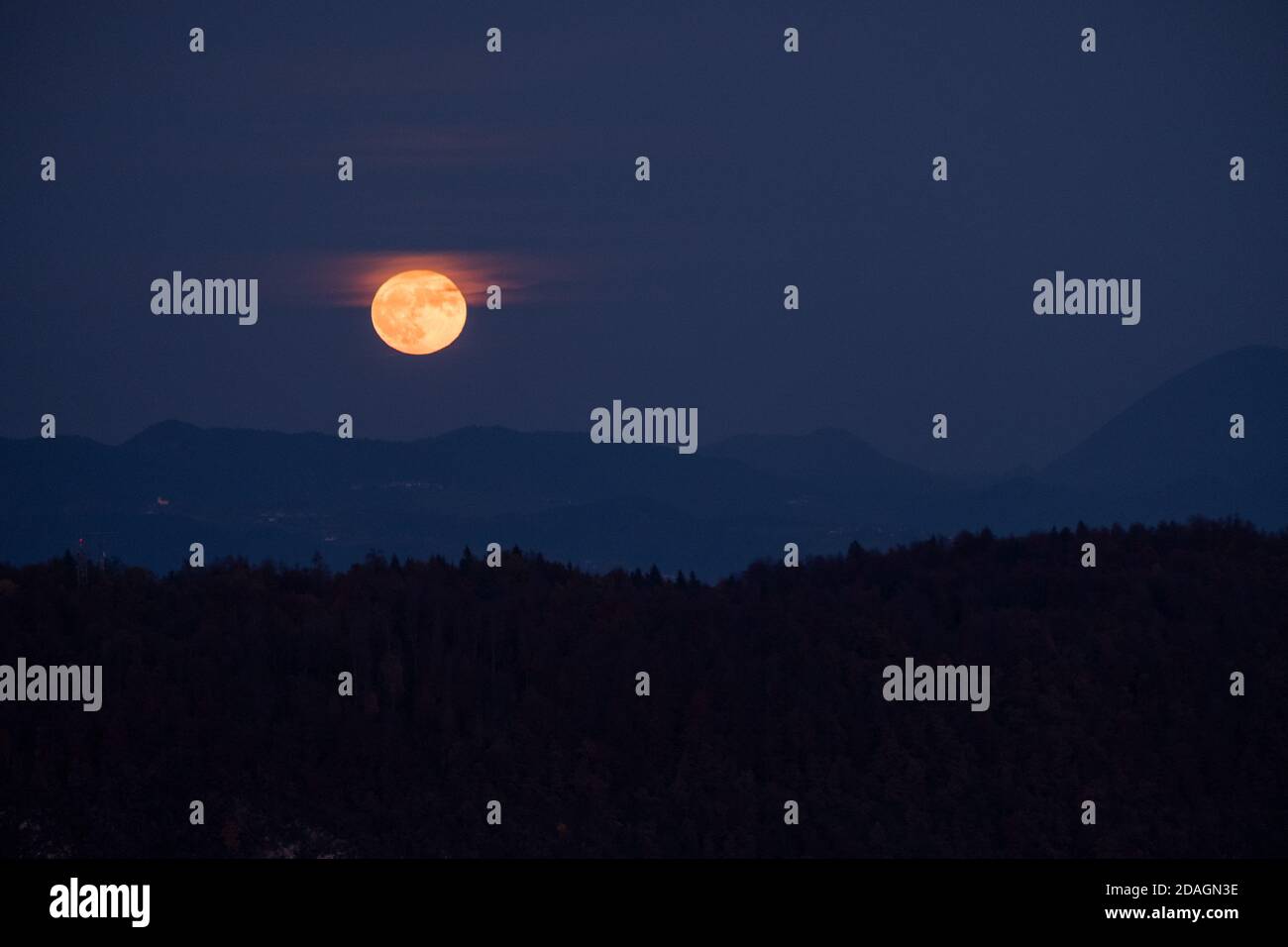 huge orange full moon rising behind a mountain ridge illuminating misty ...
