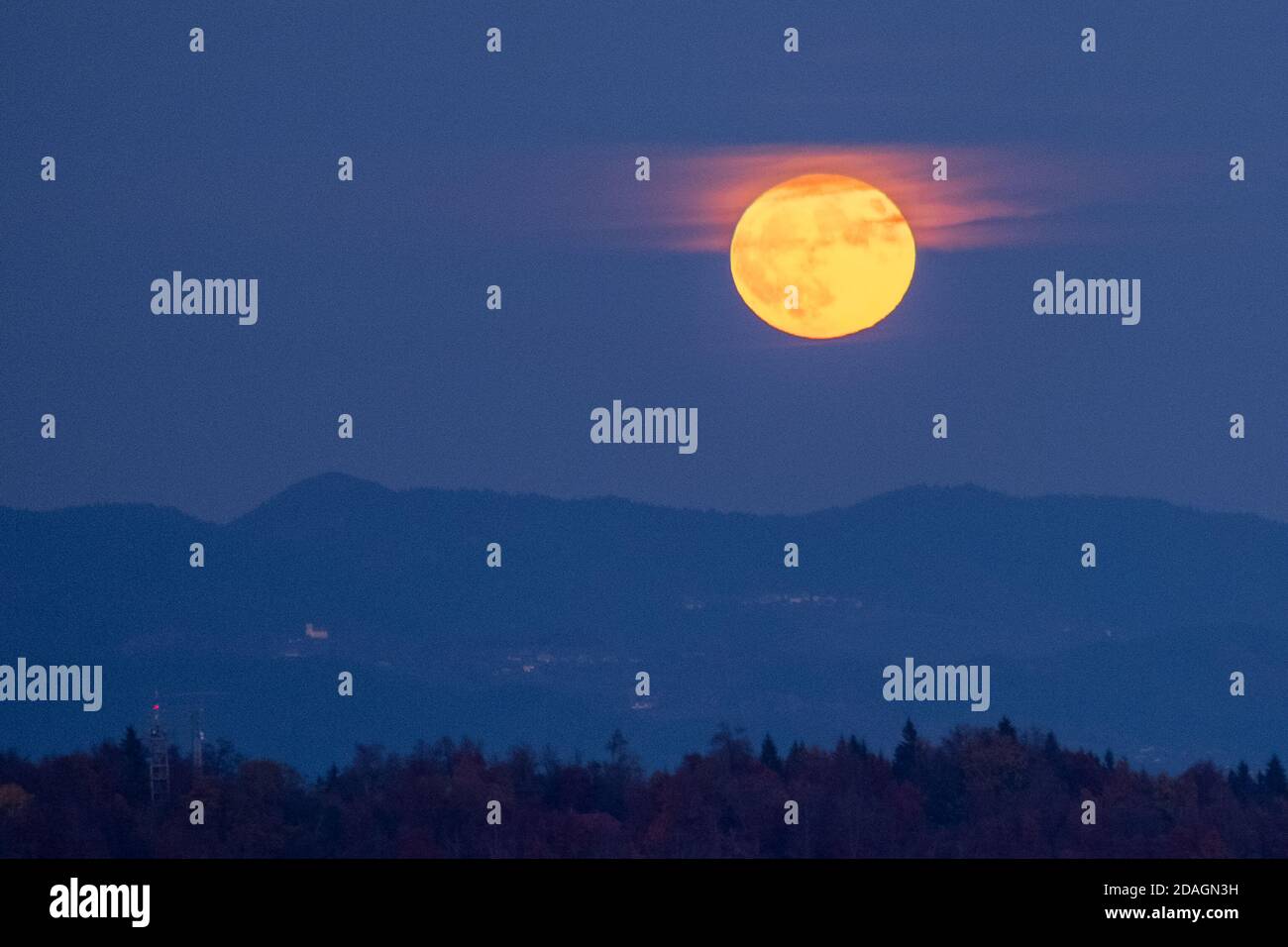 huge orange full moon rising behind a mountain ridge illuminating misty ...
