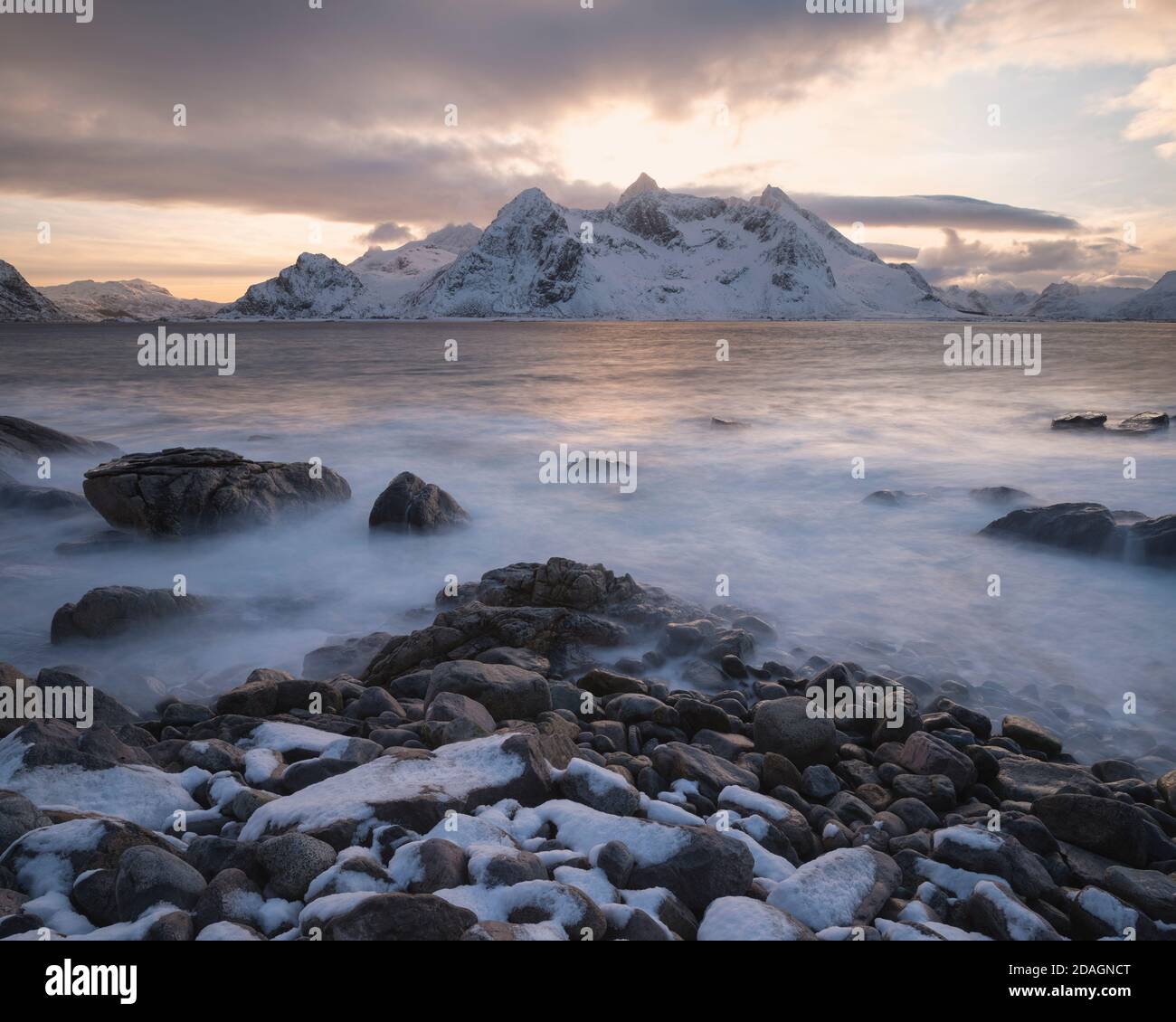 Rugged mountains of Flakstadøy rise across sea from rocky coastline at ...
