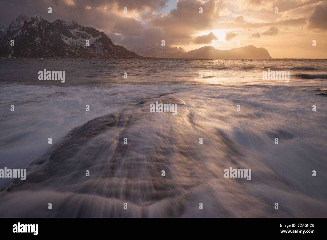 Rugged mountains of Flakstadøy rise across sea from rocky coastline at ...