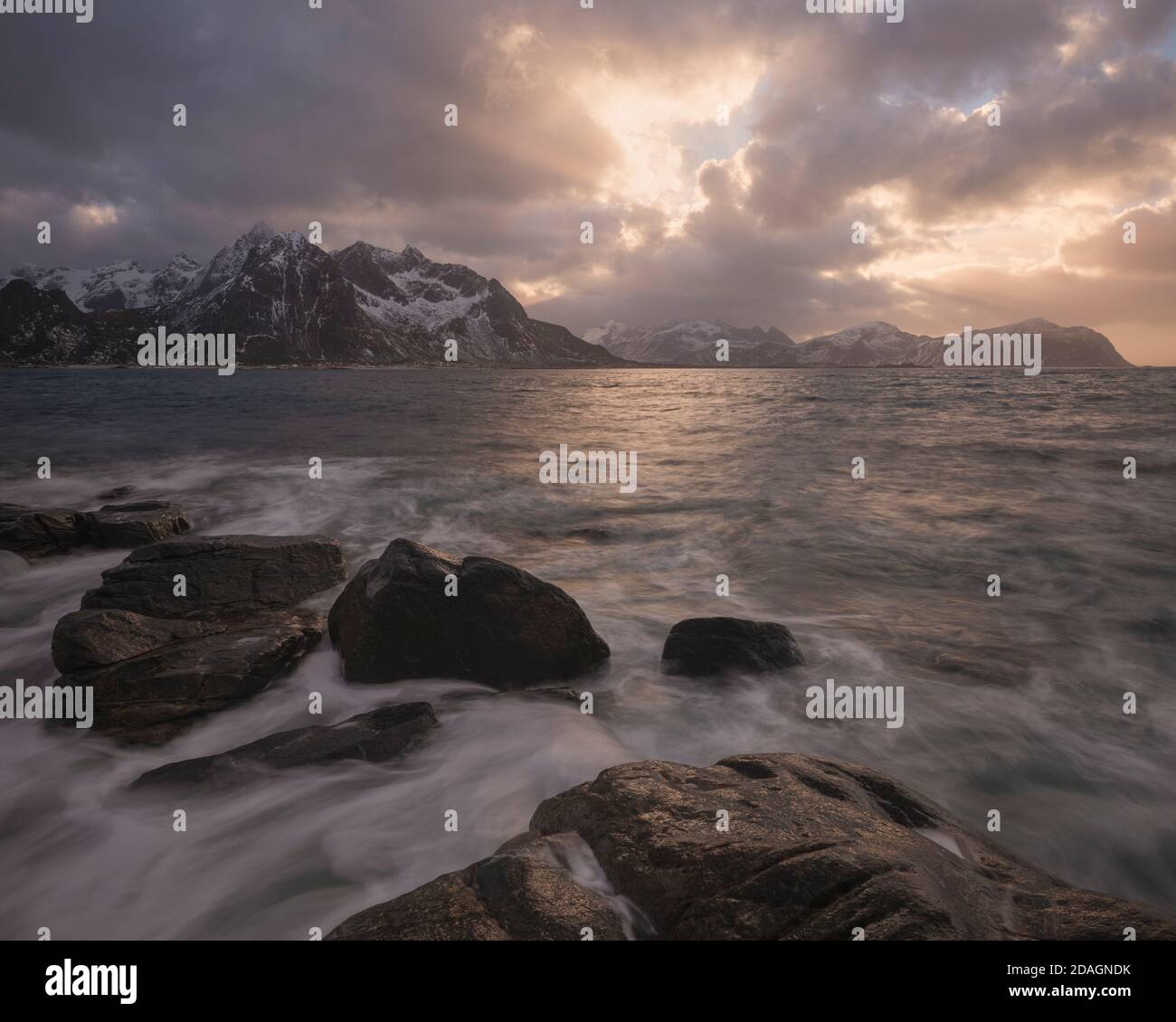Rugged mountains of Flakstadøy rise across sea from rocky coastline at ...