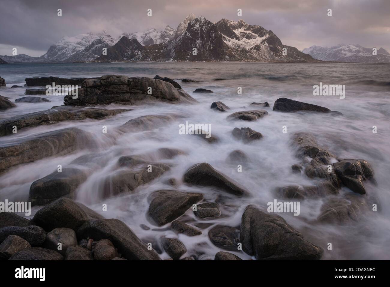 Rugged mountains of Flakstadøy rise across sea from rocky coastline at ...