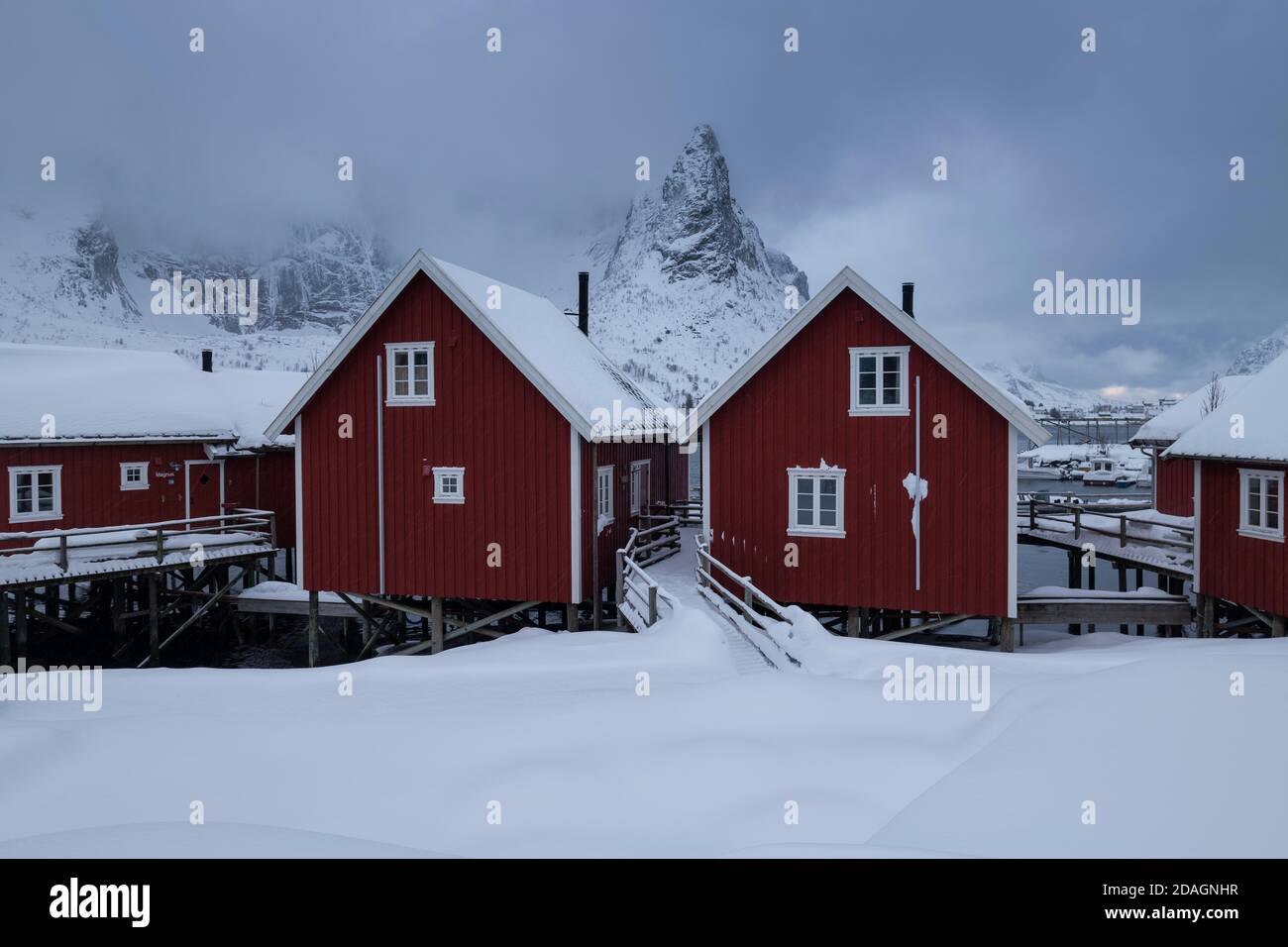 Red rorbu cabins below mountain peak in winter, Reine, Moskenesøy ...