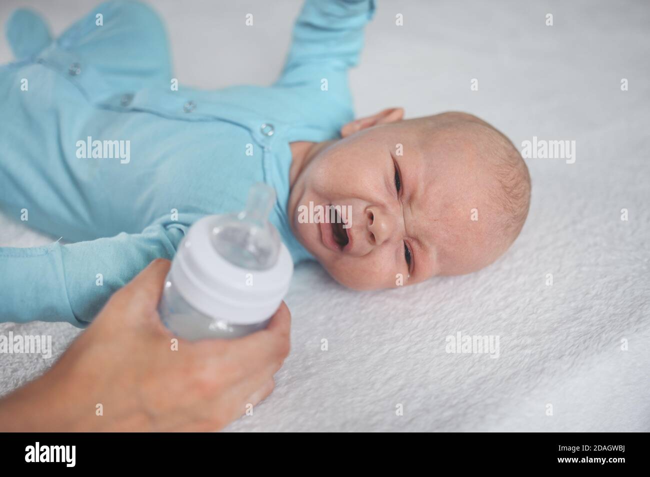 Cute emotional crying newborn boy laying on bed with milk bottle. Baby ...