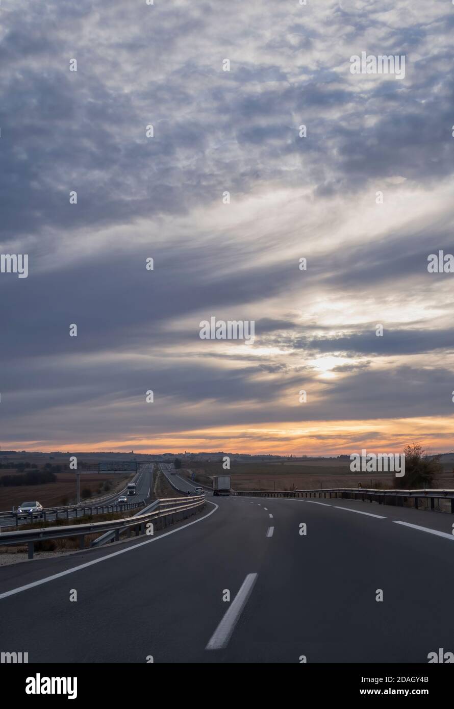 view of a curve in a motorway at a cloudy sunrise with a truck in the ...