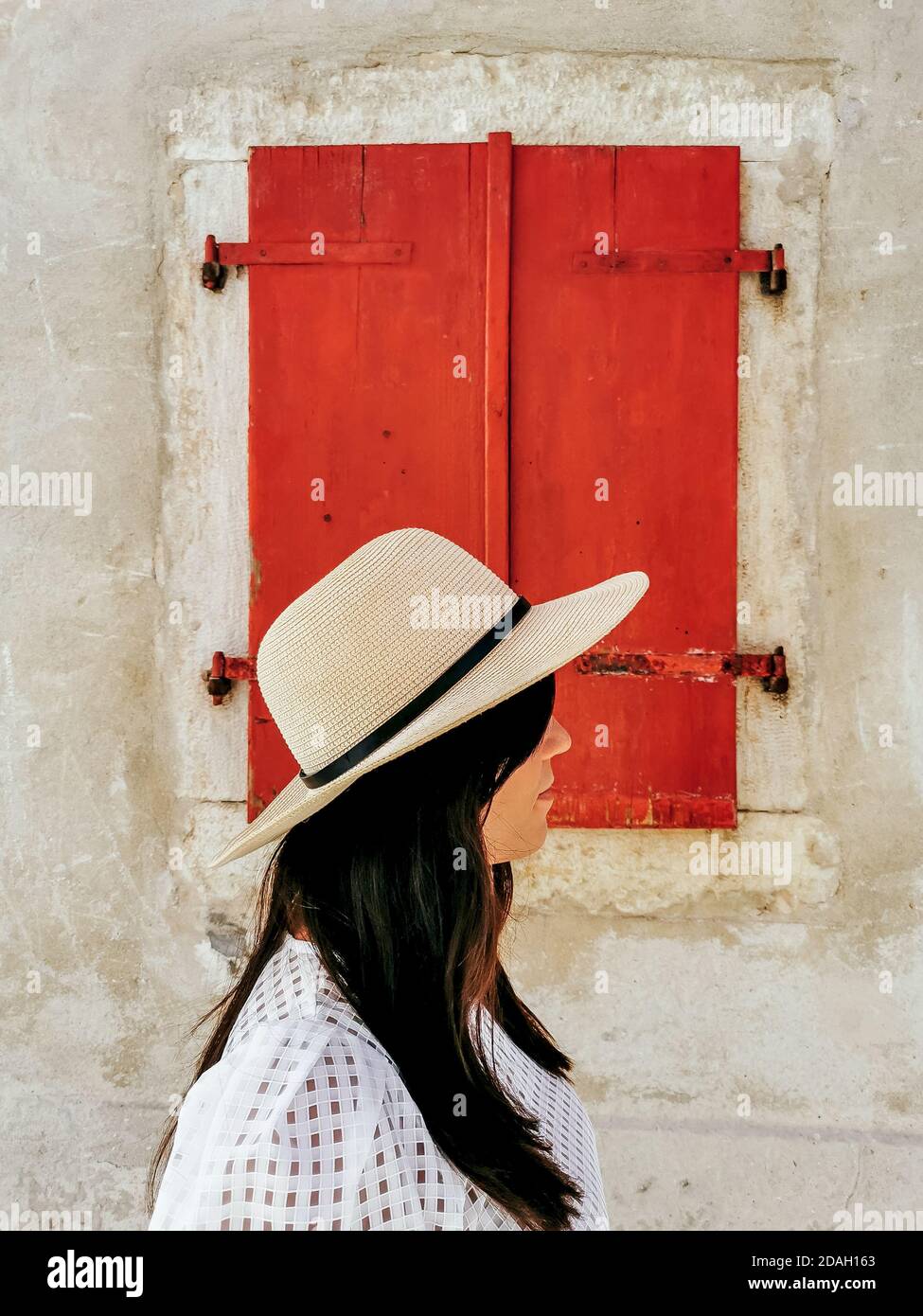 Vertical side view of a young female in a hat posing near red windows ...