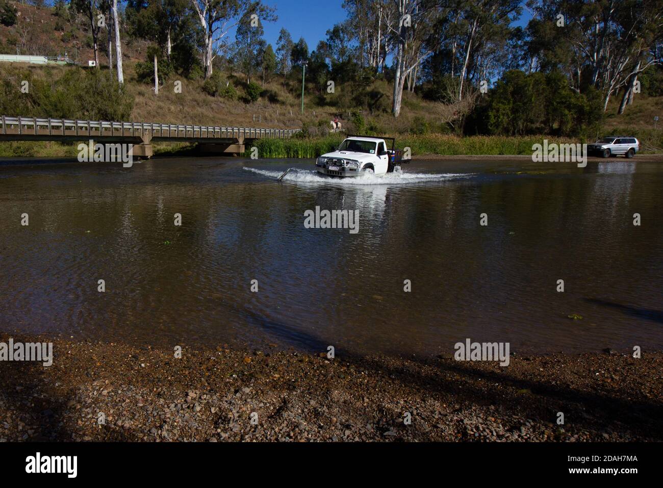 Single ute driving through a flowing river with a bridge in the ...
