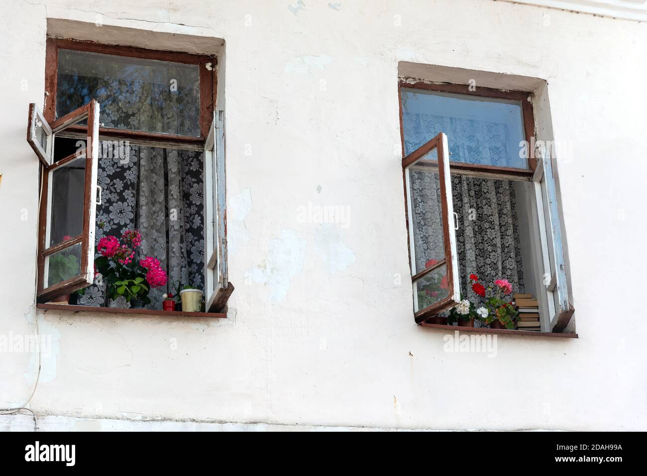 Old rustic house with open windows and blooming flowers in warm summer ...