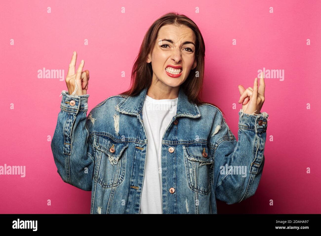 Young woman showing goat gesture, rocker horn on pink background Stock ...
