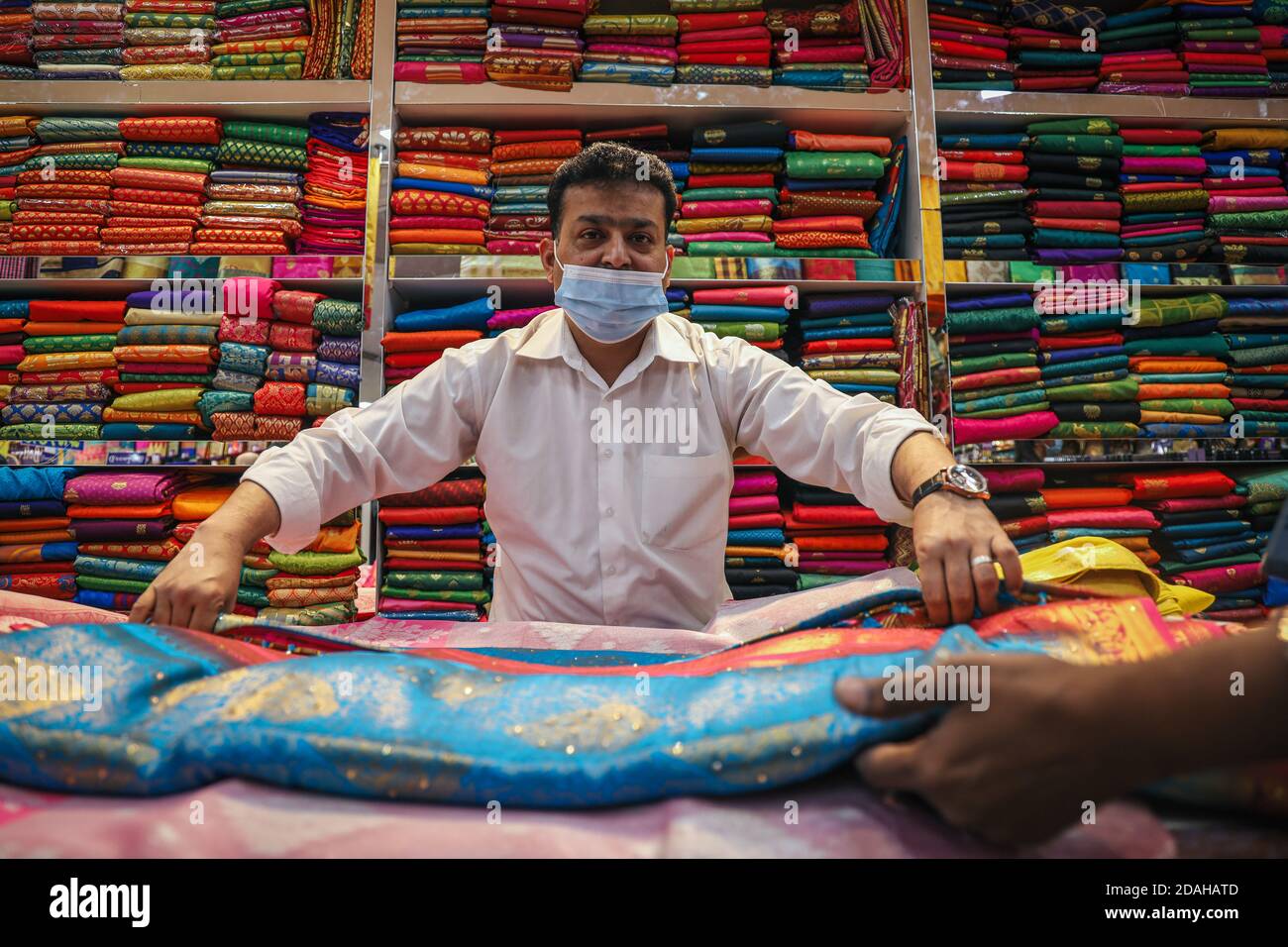 An Indian trader wearing a facemask as a precaution sells sarees ahead ...