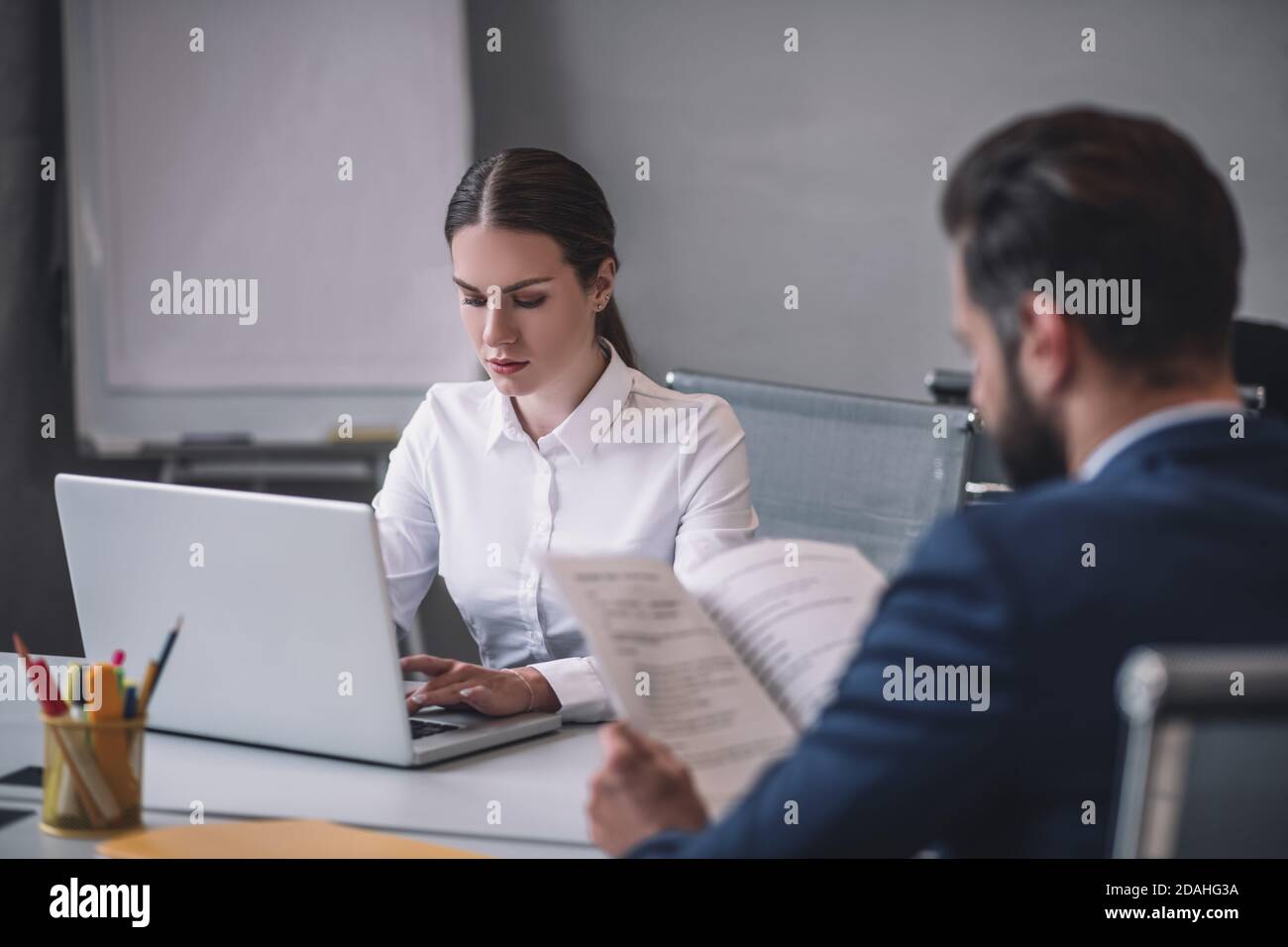 Pretty woman behind laptop and man reading opposite Stock Photo - Alamy