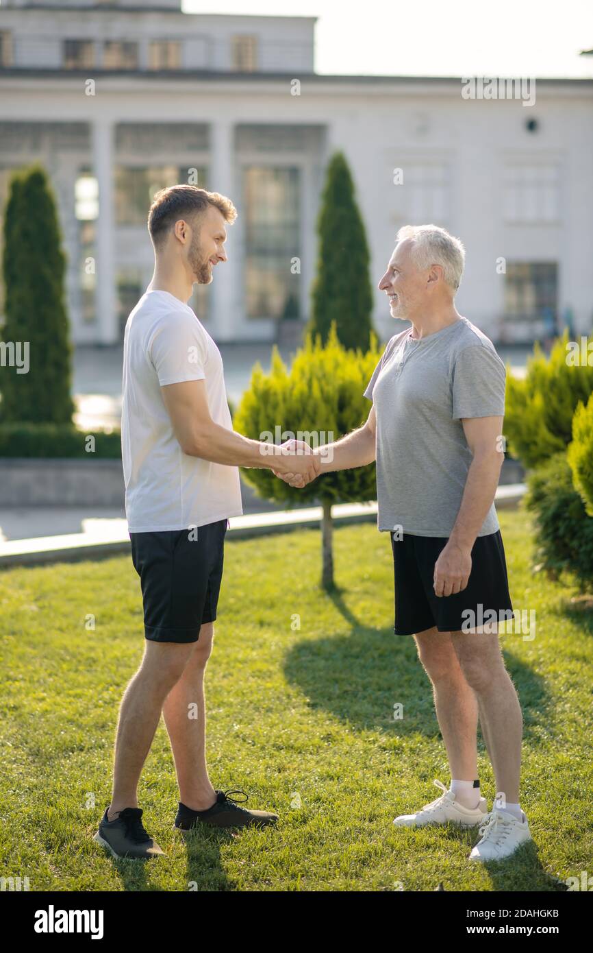 Young brown-haired male and mature grey-haired male shaking hands on ...