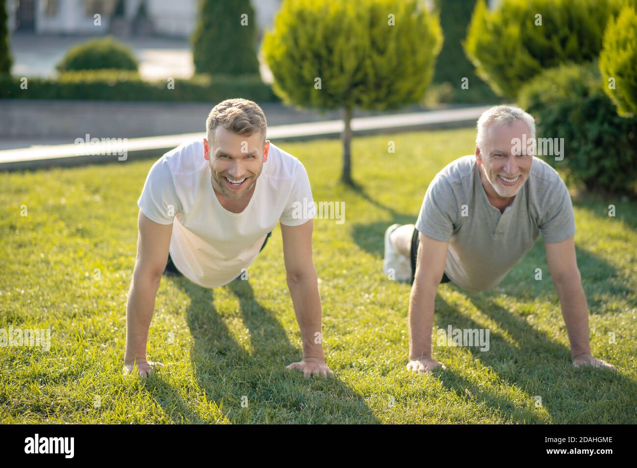 Young male and grey-haired male doing push ups on grass, smiling Stock ...