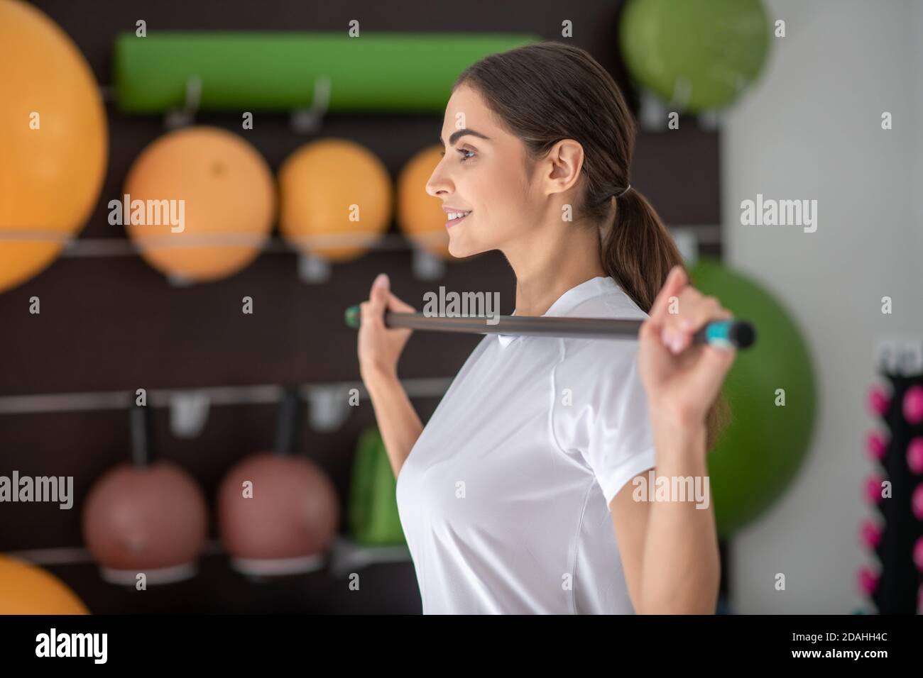 Dark-haired female exercising, holding stretching stick near her neck ...