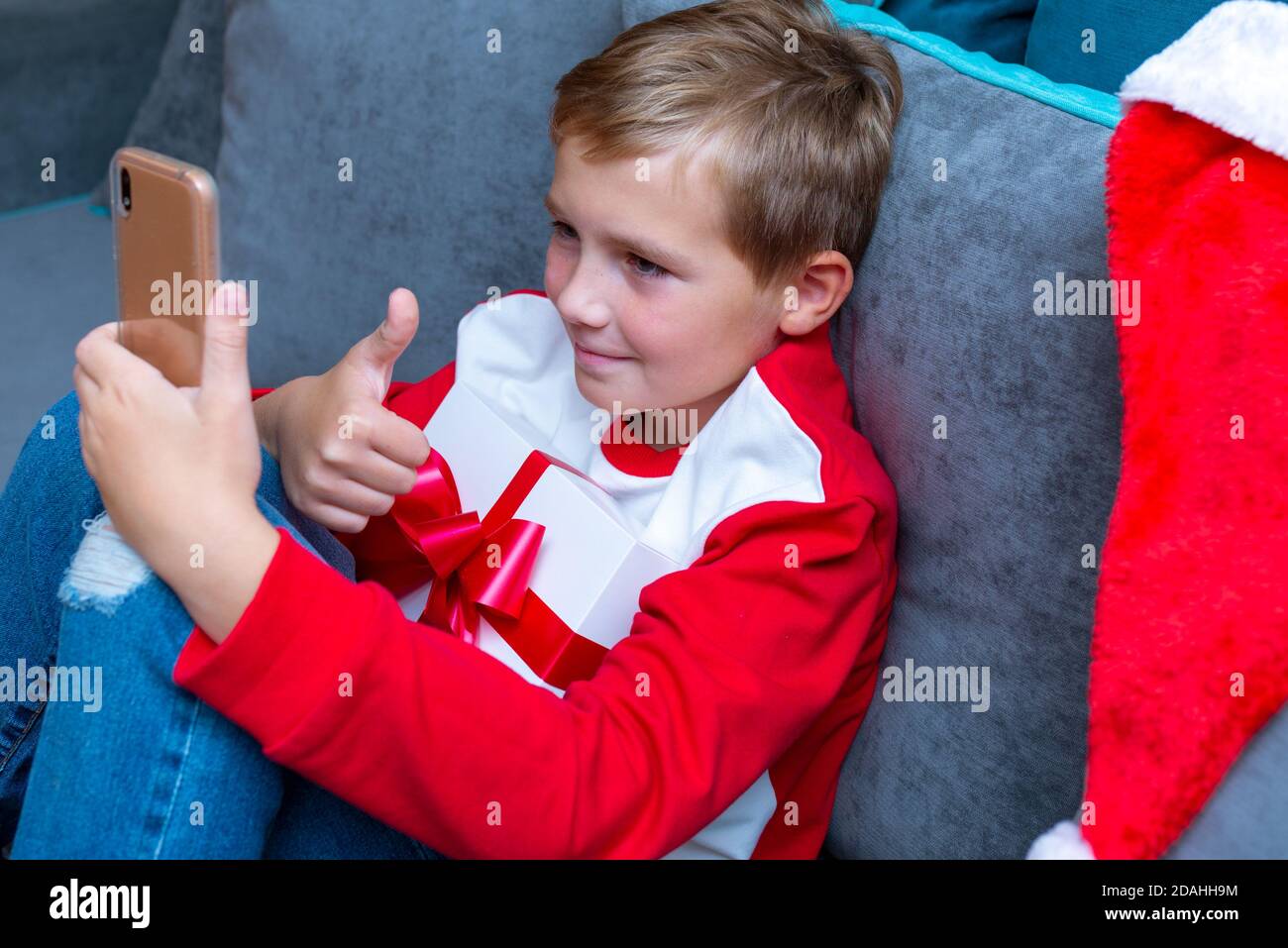 Handsome kid boy in Santa Claus hat looks at smartphone screen, shows ...