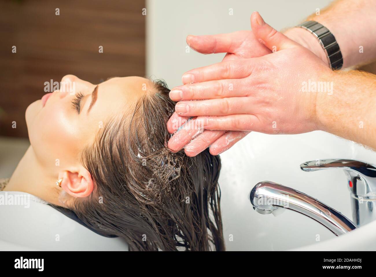 Beautiful young woman washing her hair by hands of male hairdresser in ...