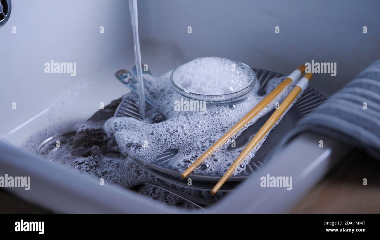 House Cleaning routine. Water streaming on dishes in kitchen sink. Hand ...