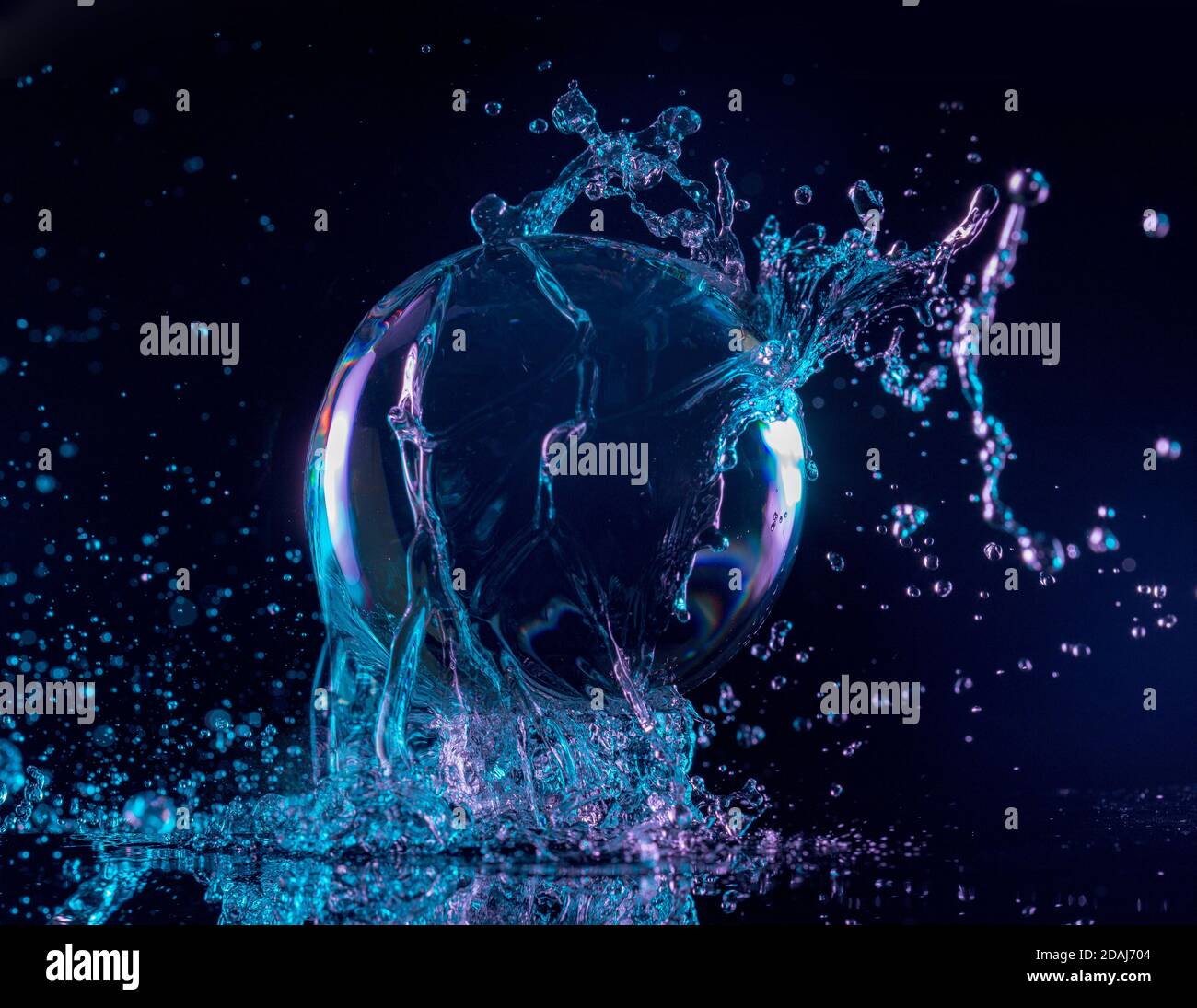 blue and purple water splashing over a transparent ball in a dark ...