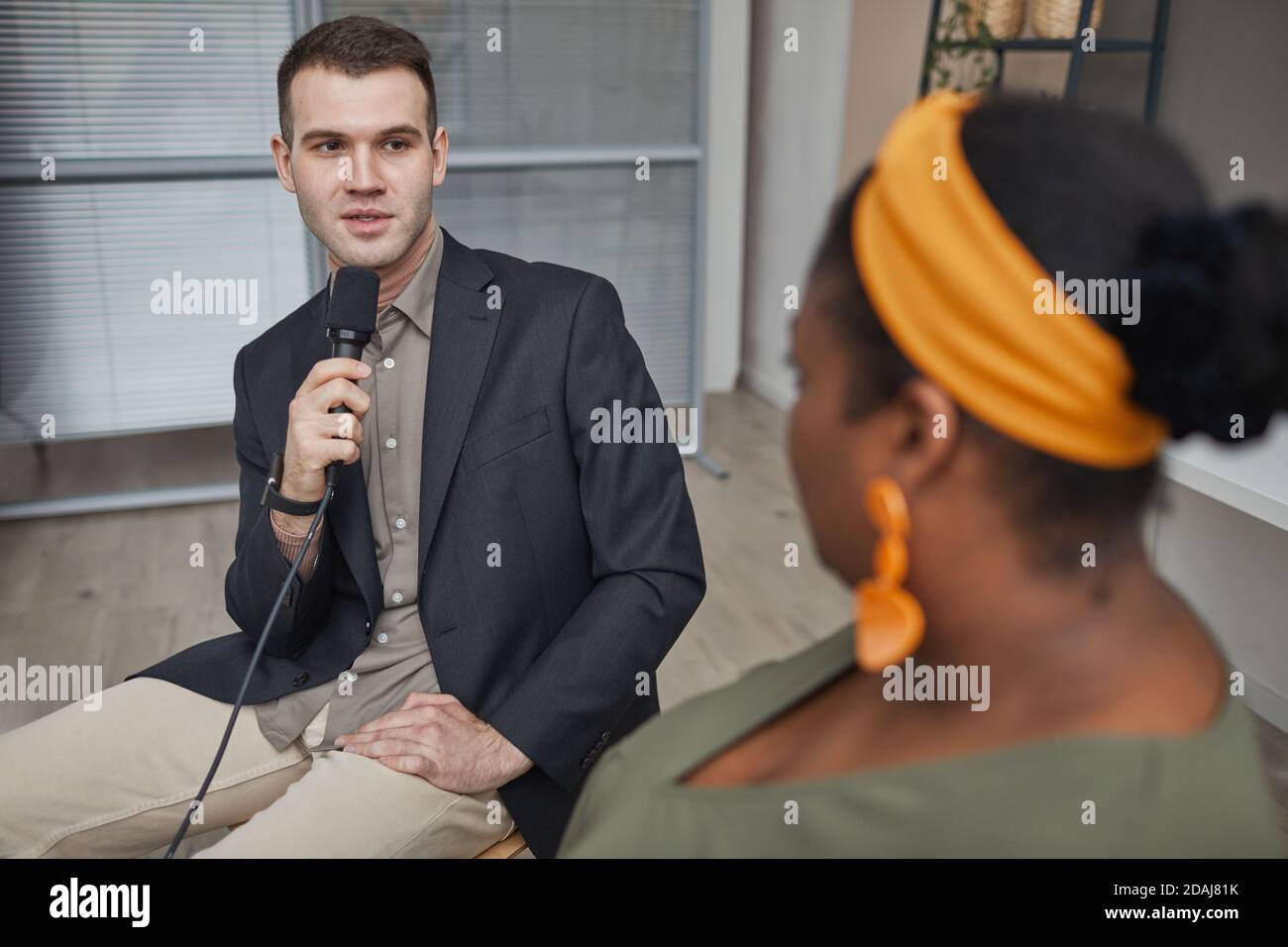Young TV reporter with microphone interviewing African woman at office ...