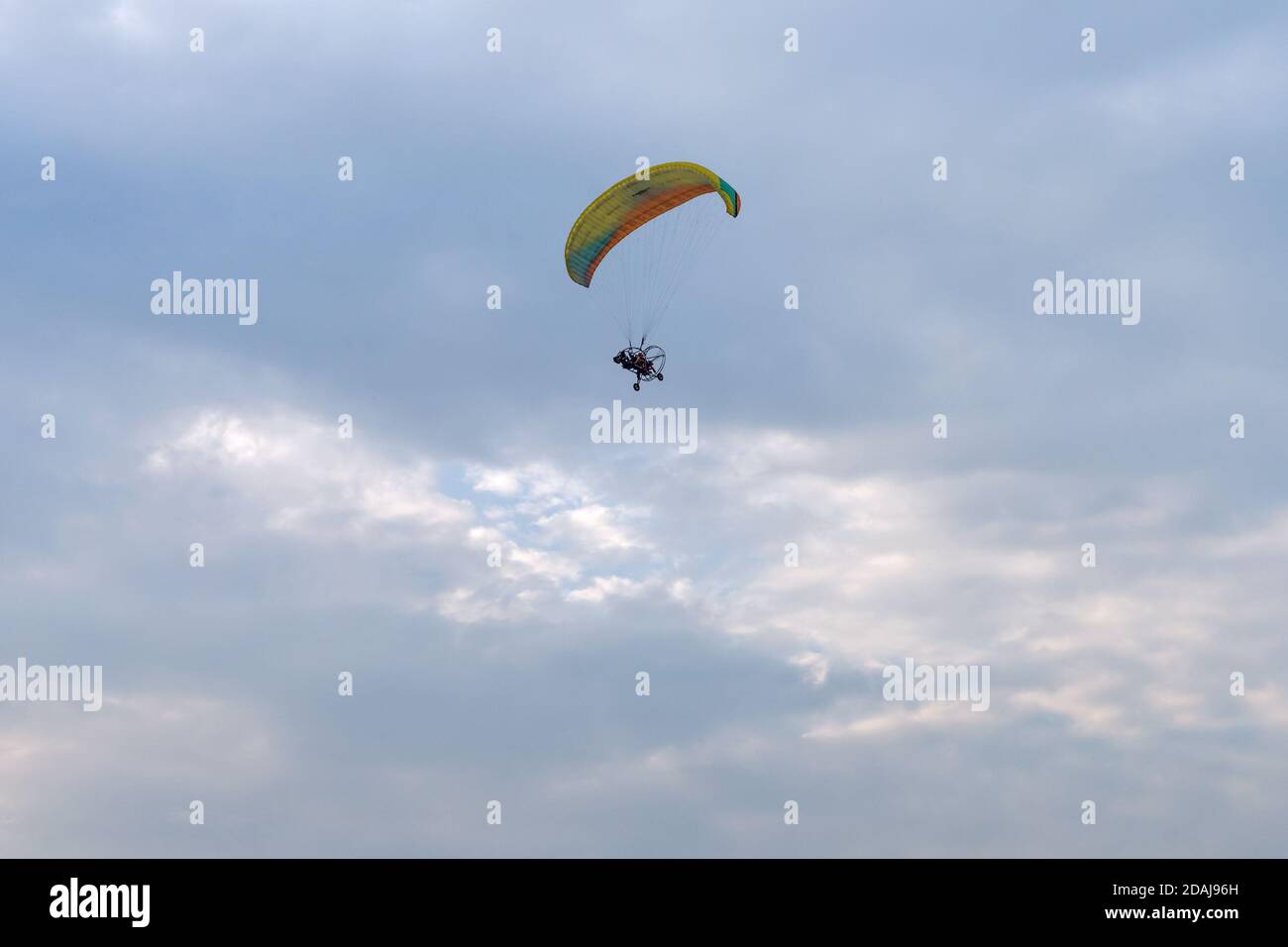 A tandem motor paraglider flies through the evening cloudy sky with two ...