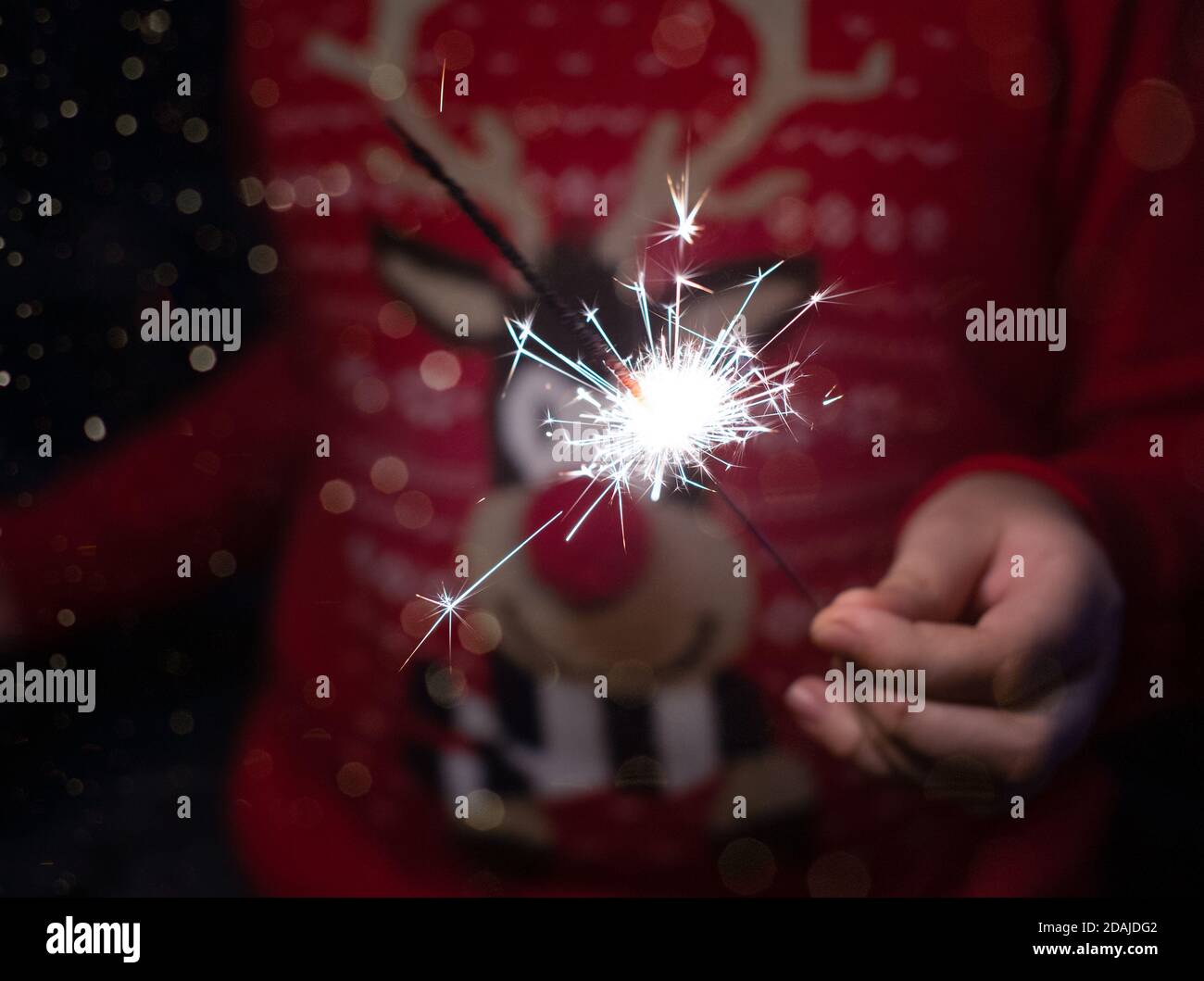 Christmas party. A child holds a lit firework on a shiny background ...