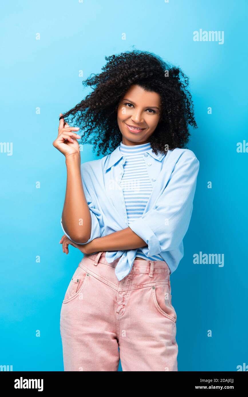 happy african american woman twirling hair on finger on blue Stock ...